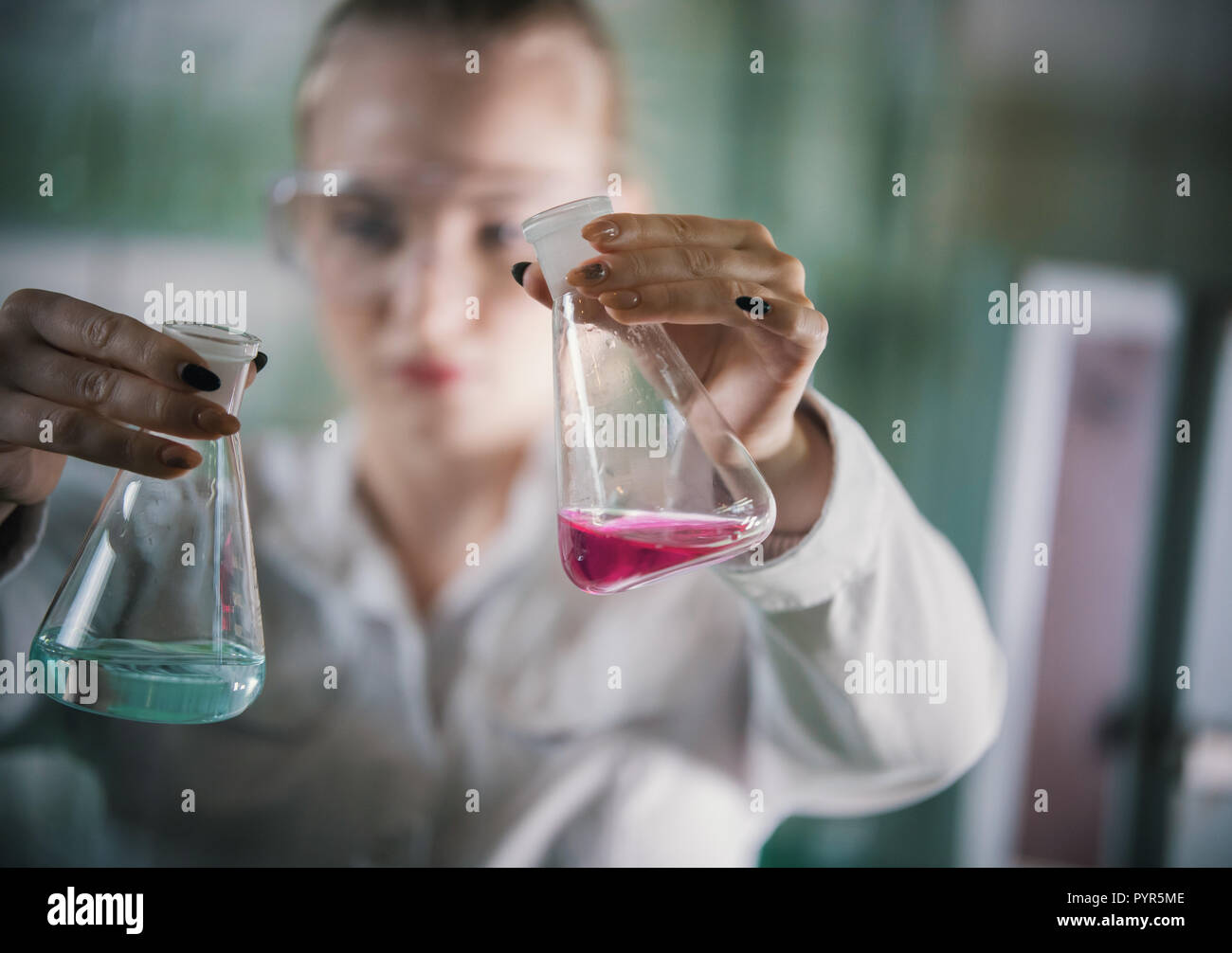Chemical laboratory. Young blonde woman holding a flasks with pink and ...