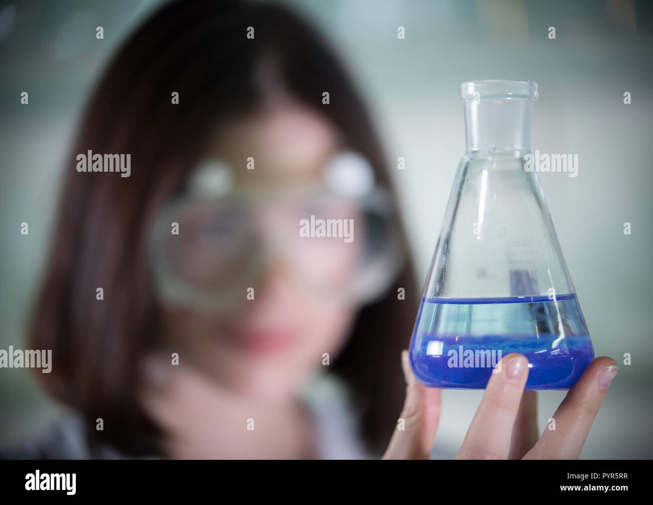 Chemical laboratory. Young woman holding a flask with blue exfoliating ...
