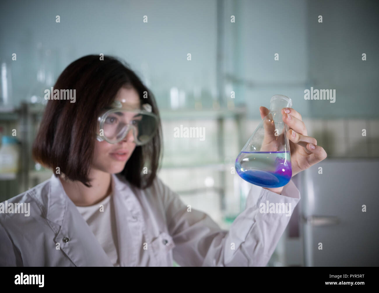 Chemical laboratory. Young woman holding a flask with blue and purple ...