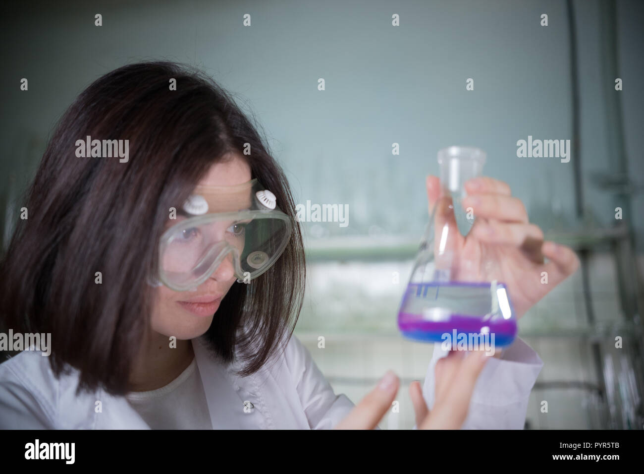 Chemical laboratory. Young woman holding a flask with blue and purple ...