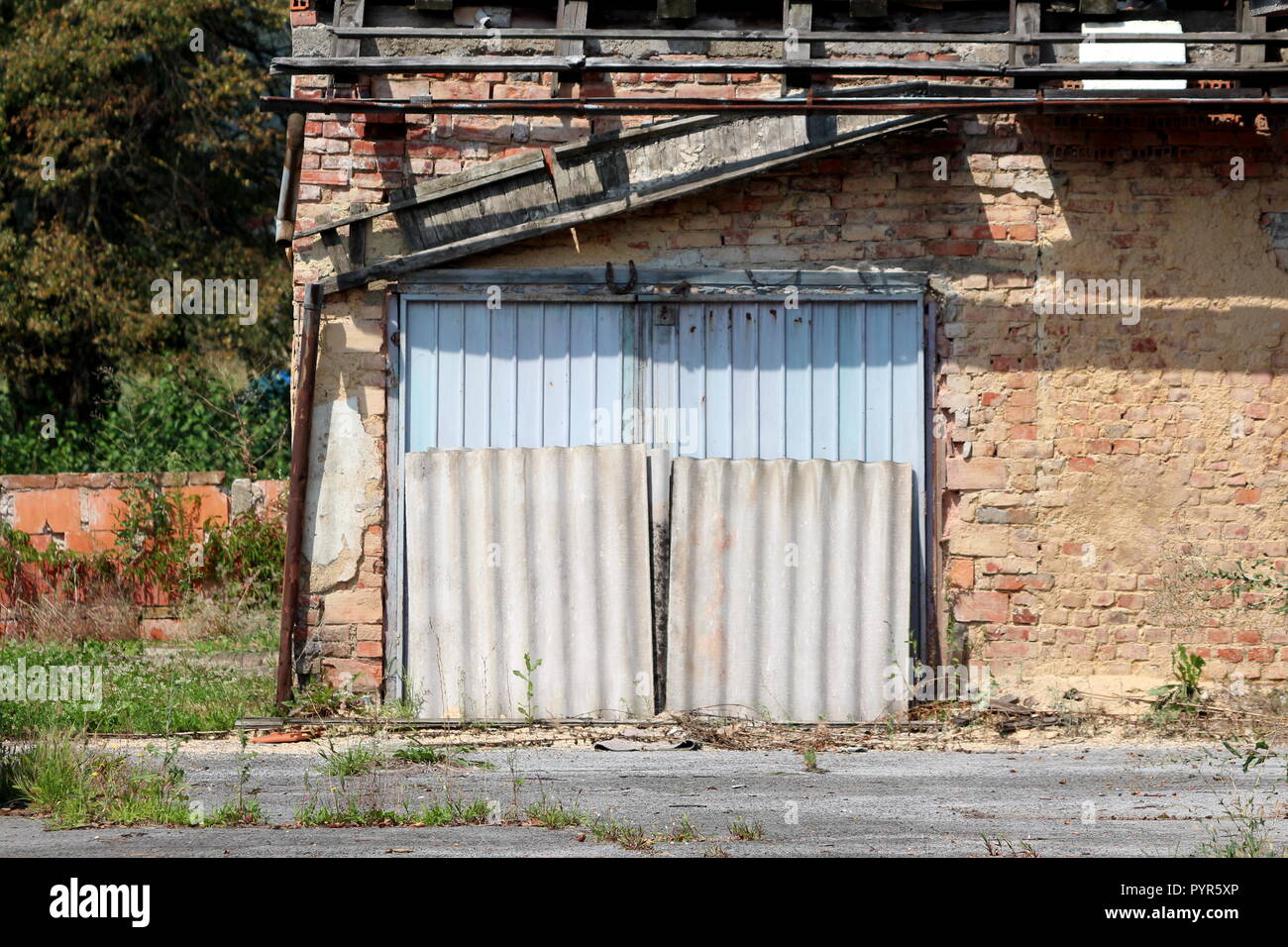Abandoned and in ruins red brick garage with metal doors blocked by ...