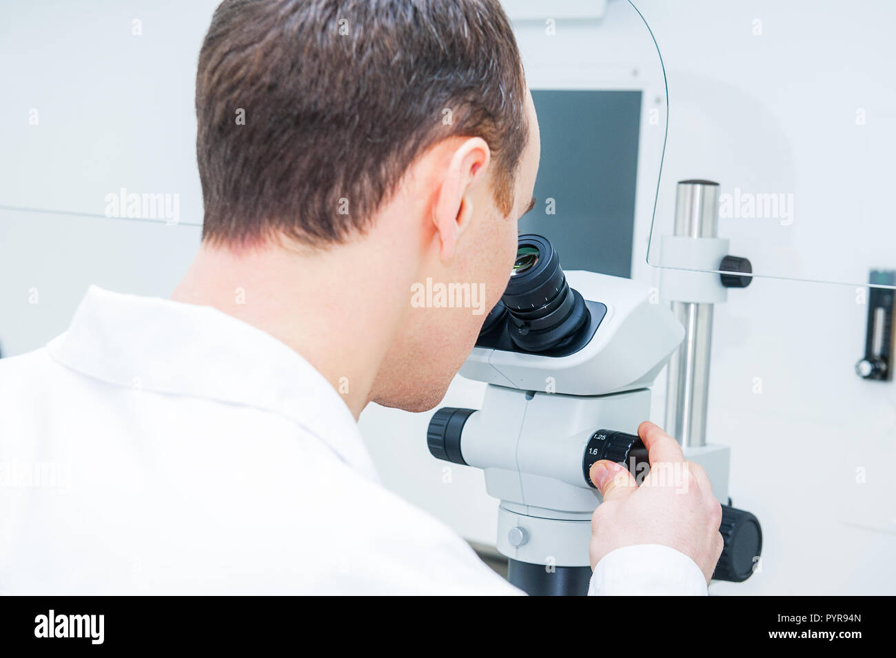 Young male medical researcher looking through microscop slide in the ...