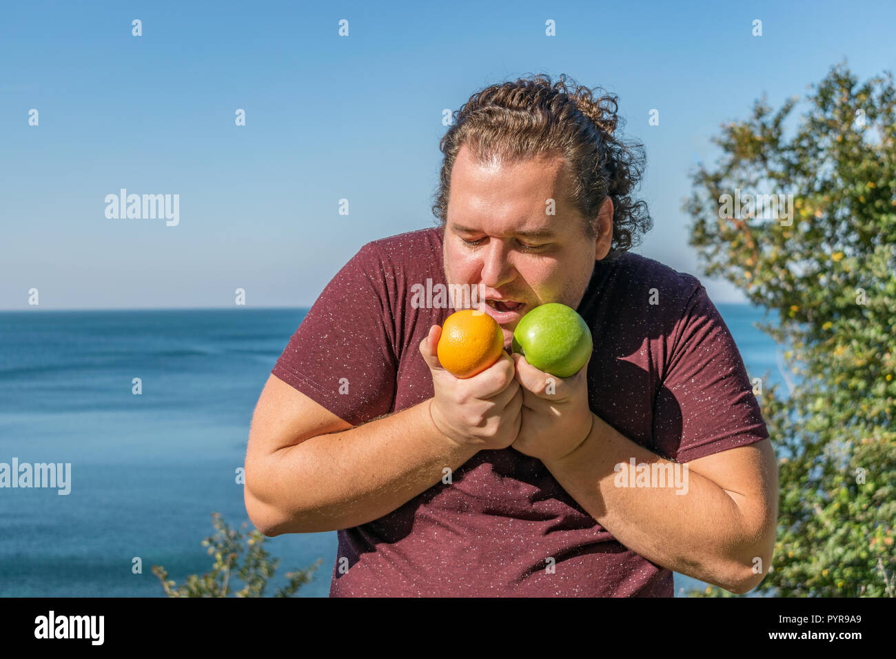 Funny fat man on the ocean eating fruits Stock Photo - Alamy
