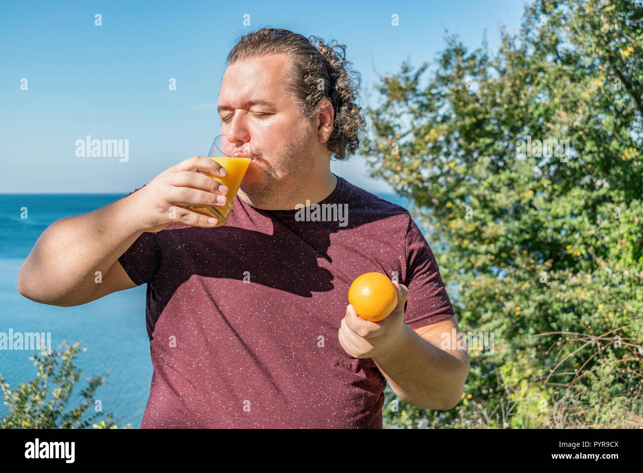 Funny fat man on the ocean drinking juice and eating fruits Stock Photo ...