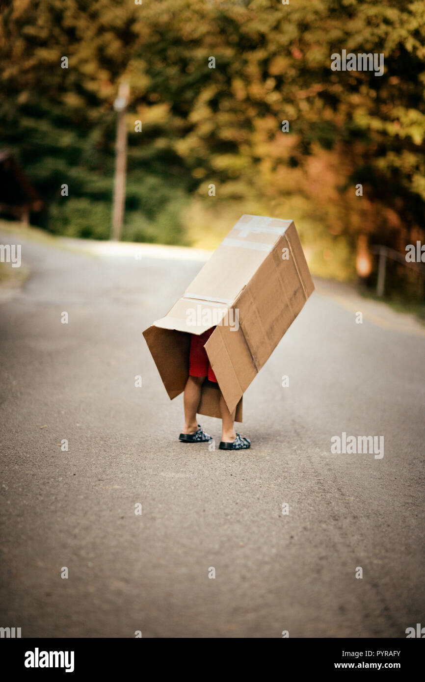 A small boy struggles to remove the box off his body while walking on ...