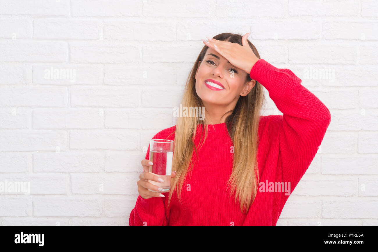 Young adult woman over white brick wall drinking glass of water ...