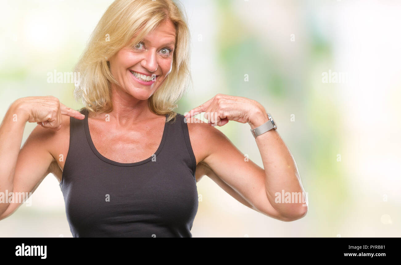 Middle age blonde woman over isolated background looking confident with smile on face, pointing ...