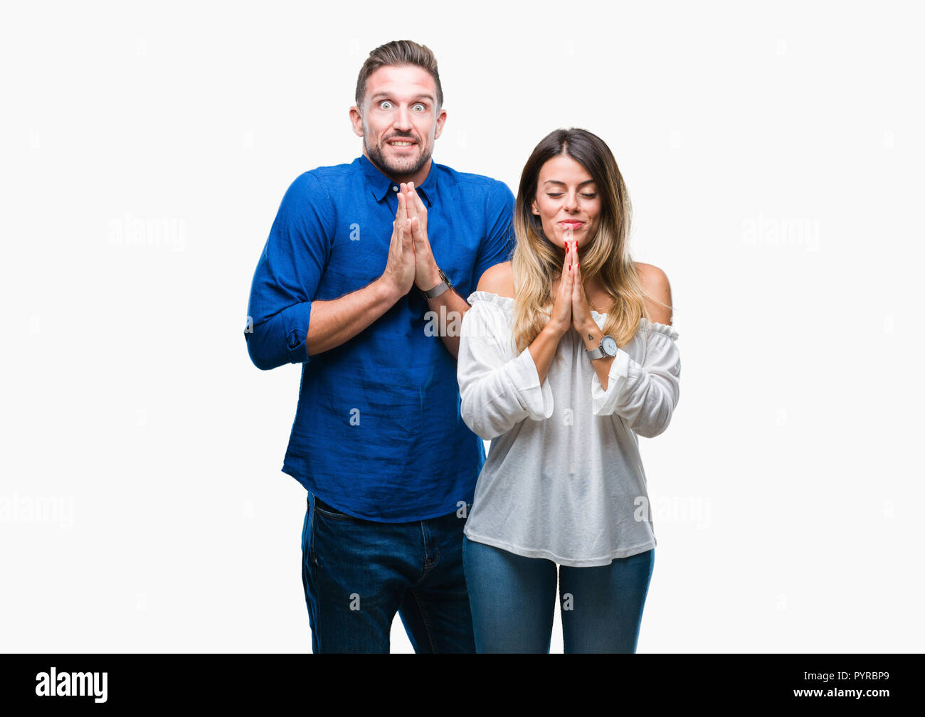 Young couple in love over isolated background praying with hands ...