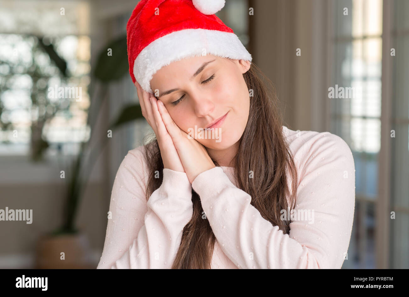 Beautiful young woman wearing Santa Claus hat at home sleeping tired ...