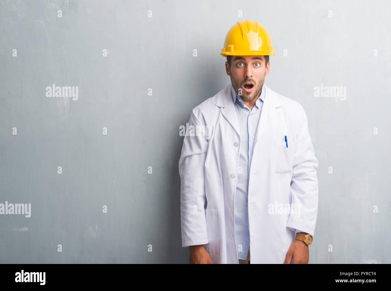 Handsome young engineer man over grey grunge wall wearing safety helmet ...