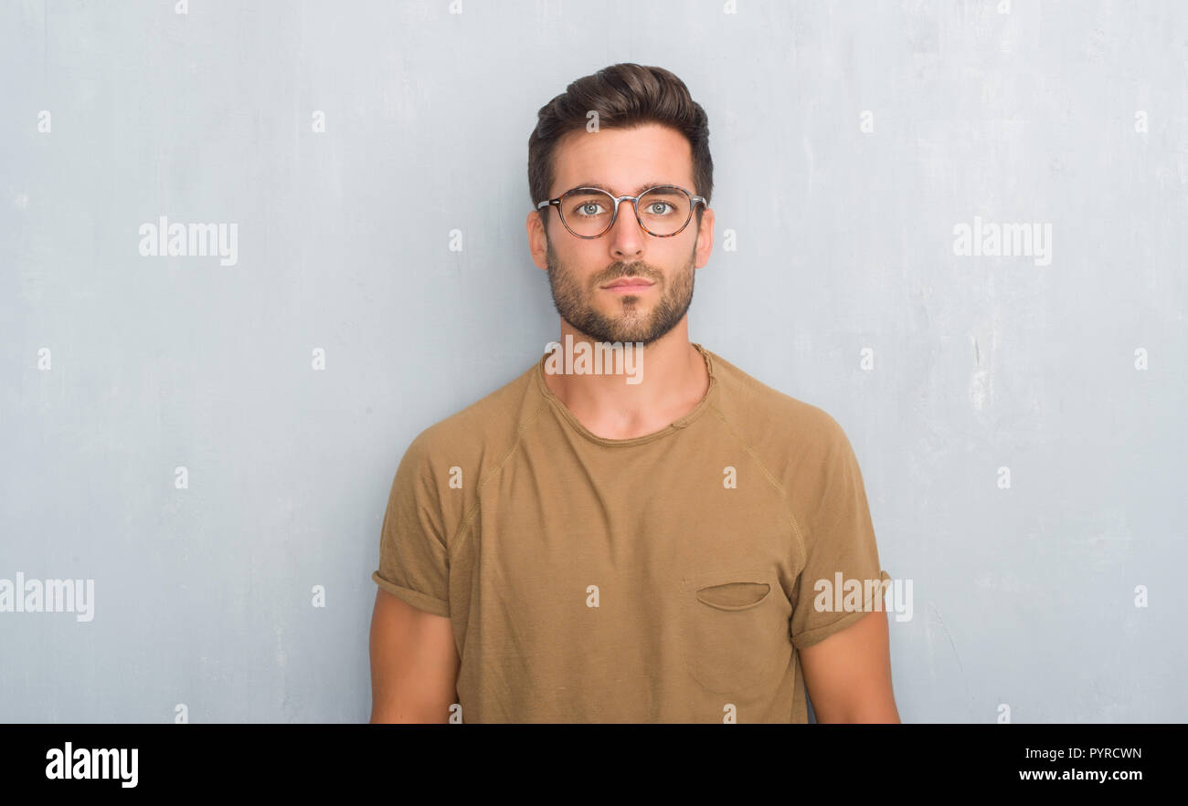 Handsome Young Man Over Grey Grunge Wall Wearing Glasses With Serious