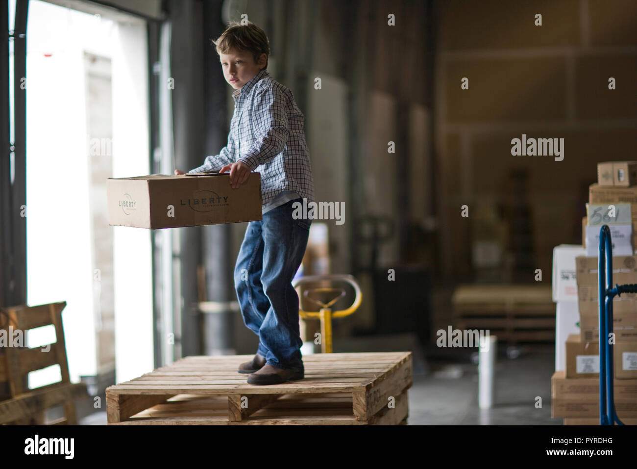 Young boy holding a cardboard box while standing on a wooden platform ...