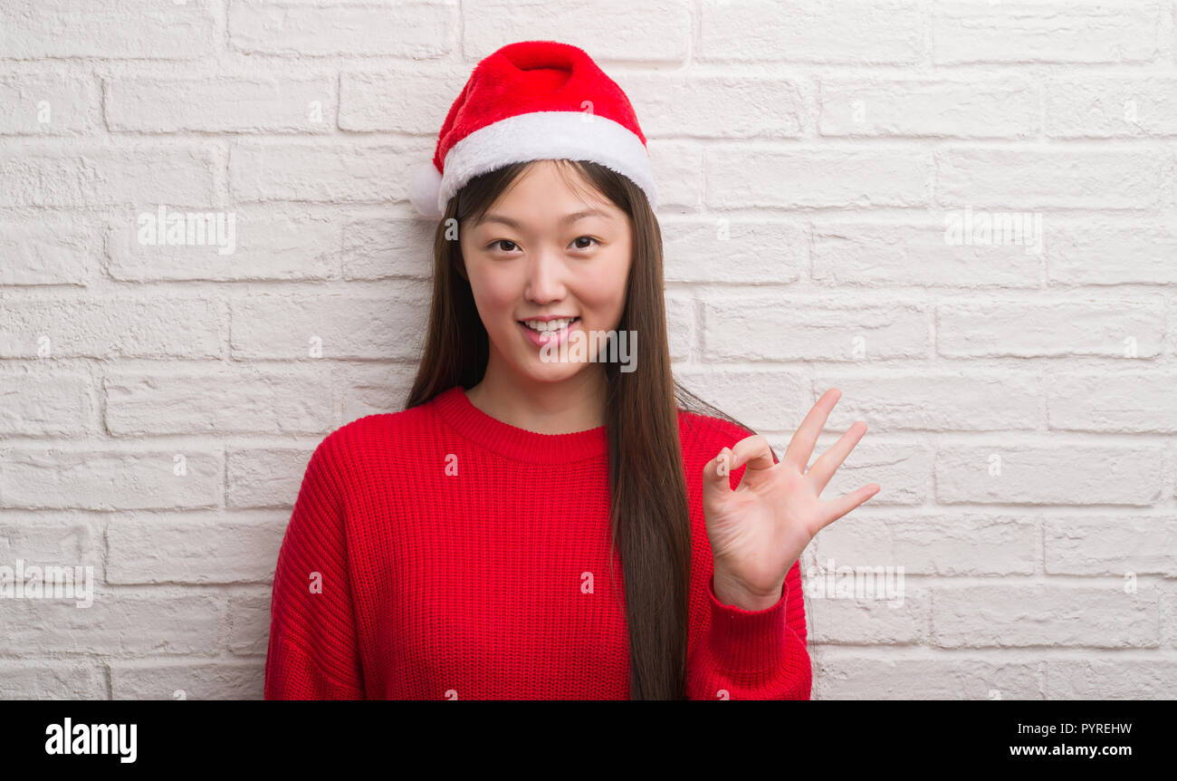 Young Chinese woman wearing Santa Claus hat doing ok sign with fingers ...