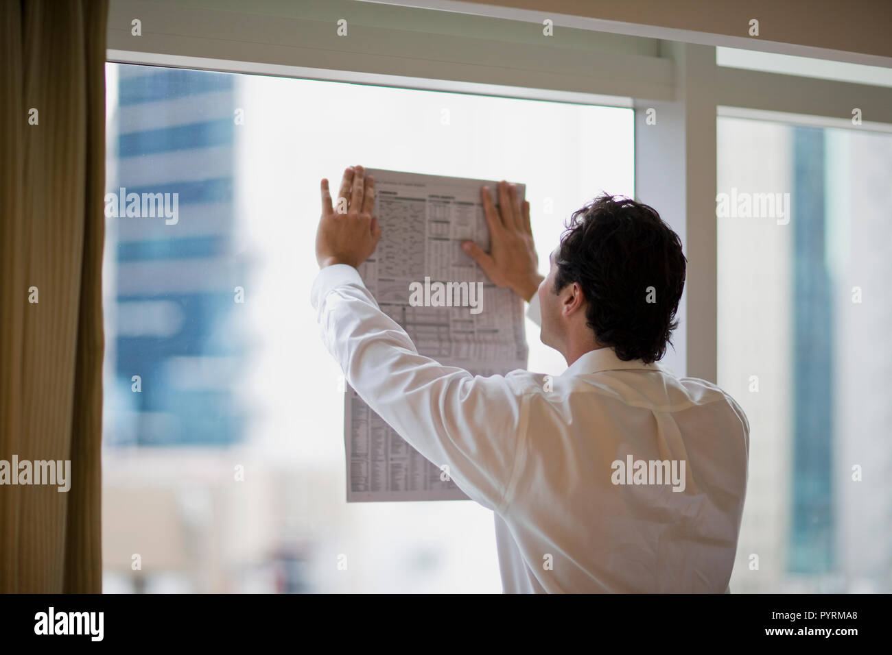 Young businessman holding a newspaper against a window while standing ...