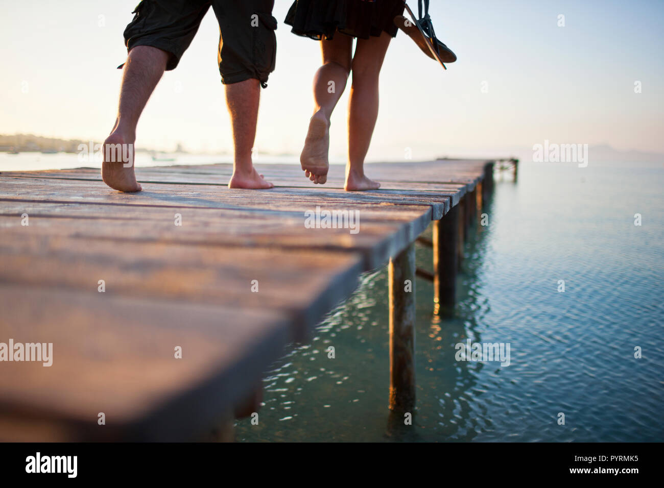 Two pairs of legs dangling off a wooden pier Stock Photo - Alamy