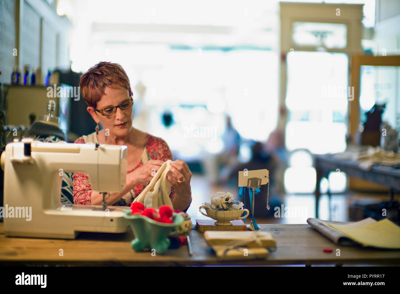 Mature female dressmaker making clothes while sitting at a sewing ...