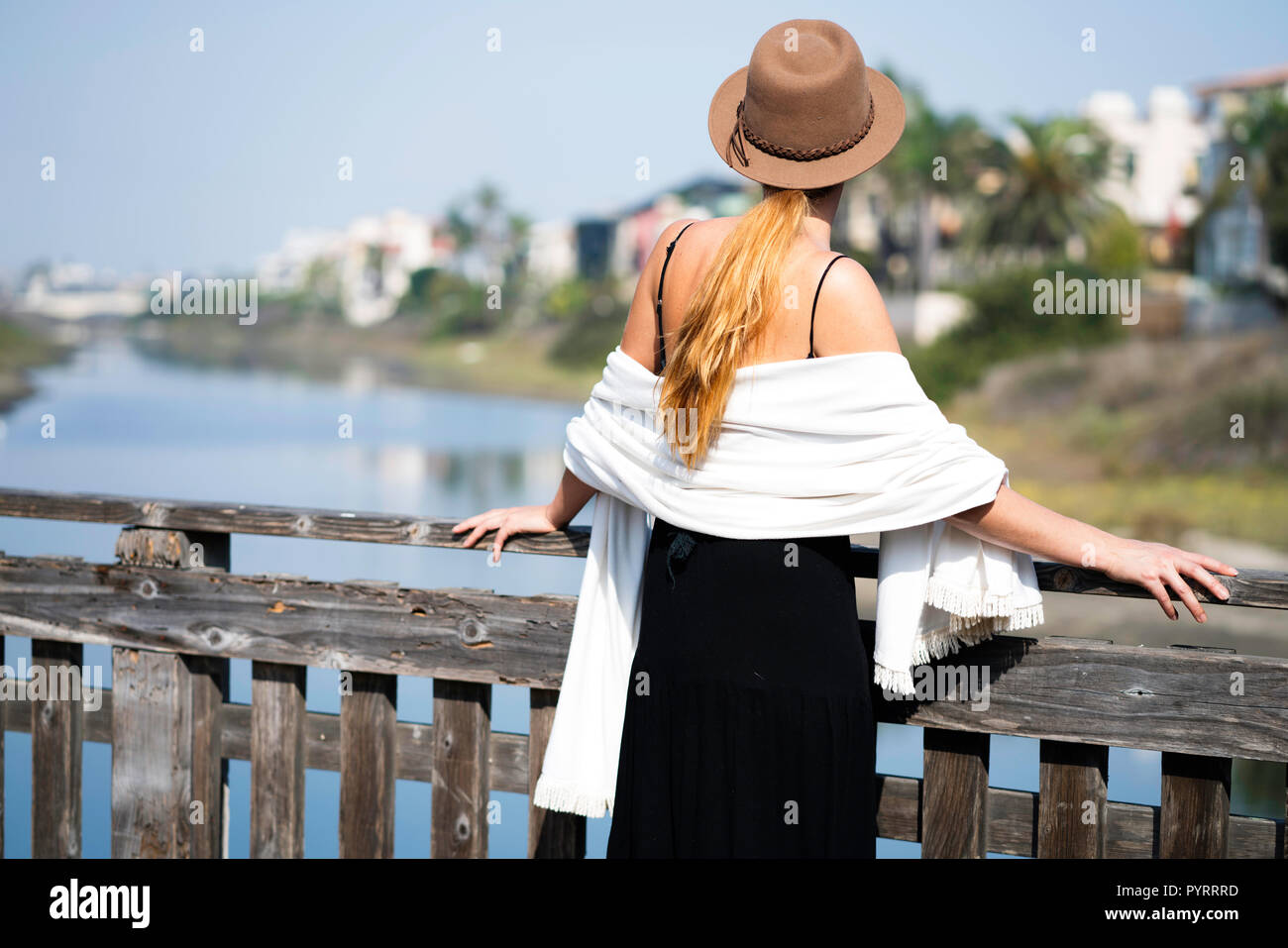 Female model poses by water with a brown hat, black dress and white ...
