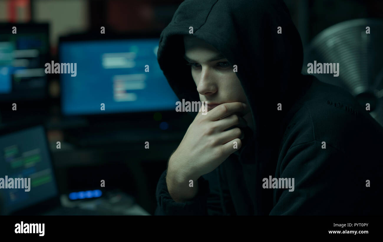 Young hacker with a hoodie thinking with hand on chin and working with ...