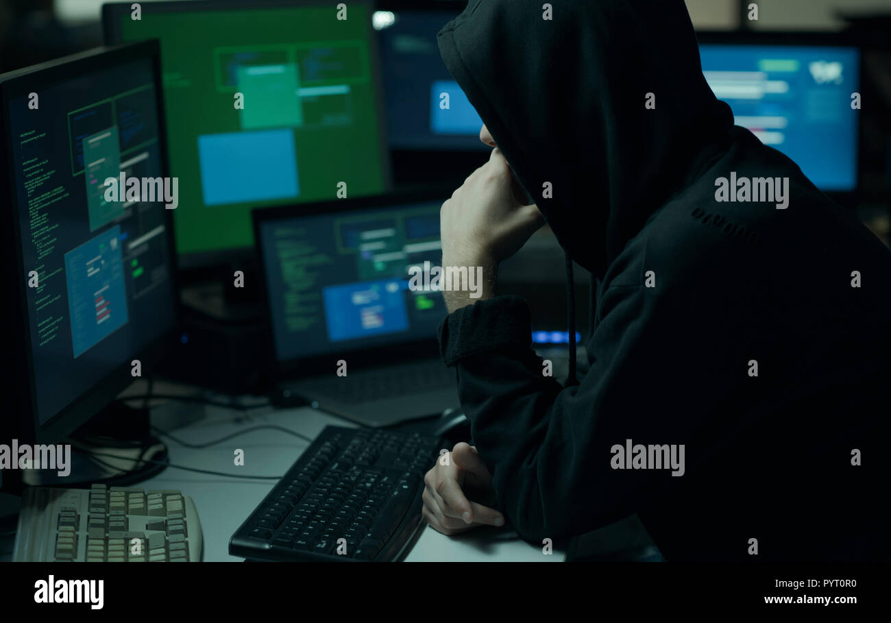 Young hacker with a hoodie thinking with hand on chin and working with ...