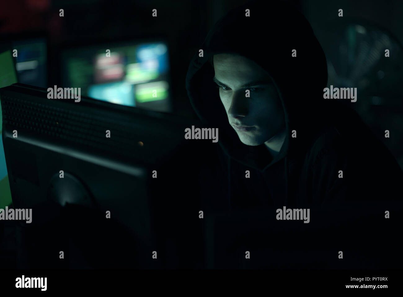 Young professional hacker working in a dark office with computers ...