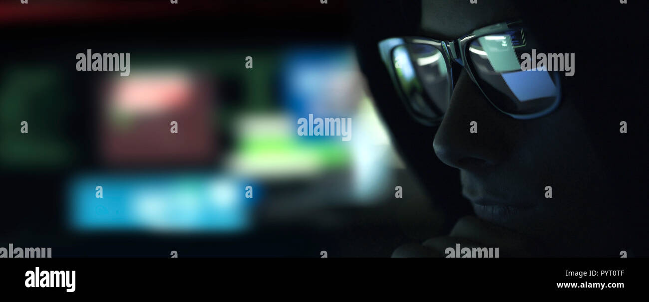 Nerd hacker with glasses working with a computer in the dark ...