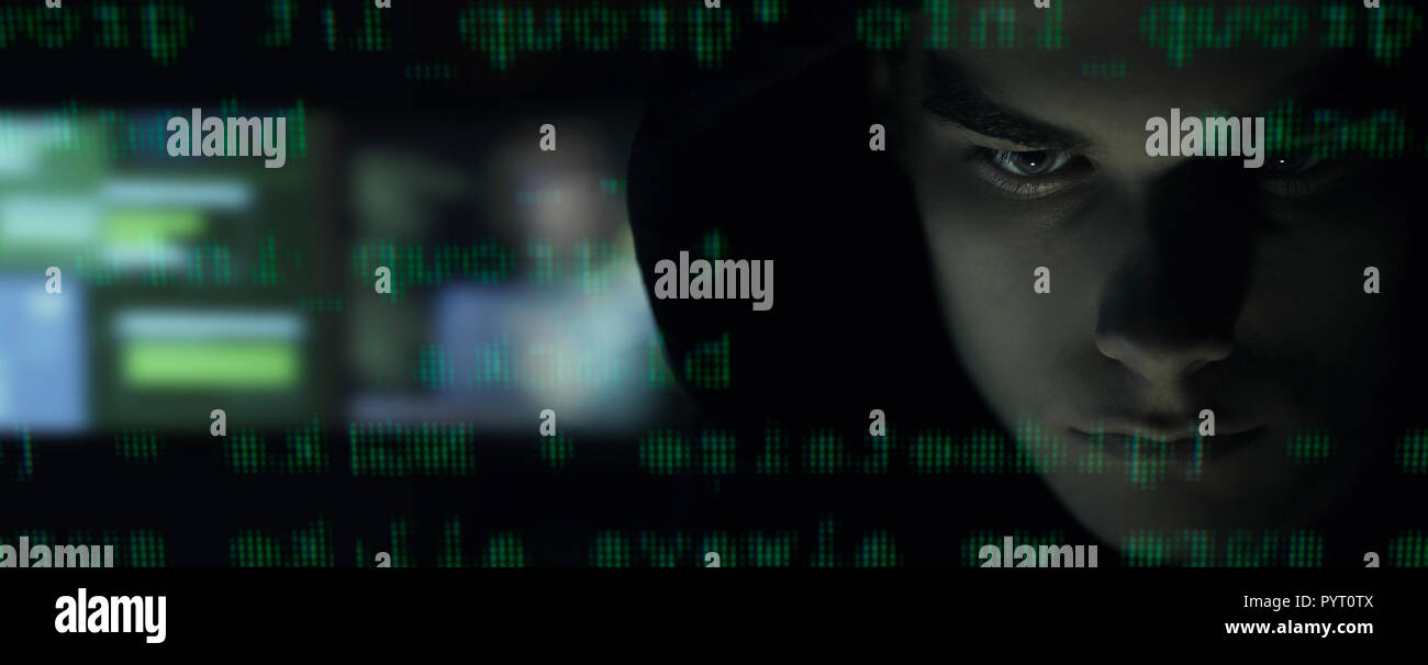 Cool young hacker with hoodie posing in the dark and programming code ...