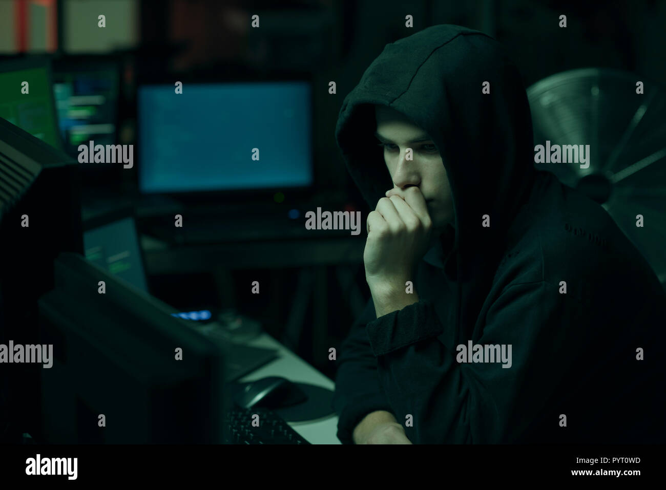 Young hacker with a hoodie thinking with hand on chin and working with ...