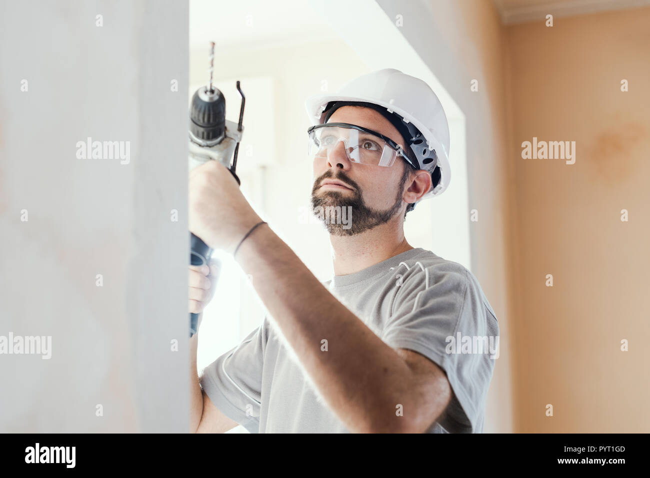 Professional construction worker using a drill, he is wearing a safety ...