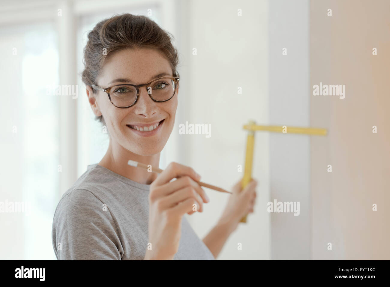 Smiling young woman doing a home makeover, she is measuring a wall ...