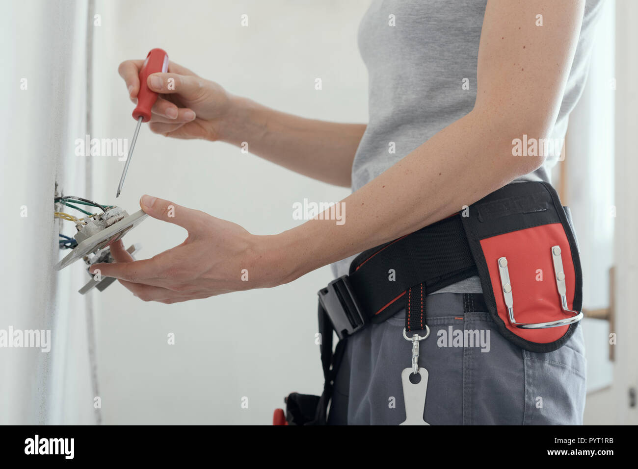Professional female electrician fixing a socket at home using a ...