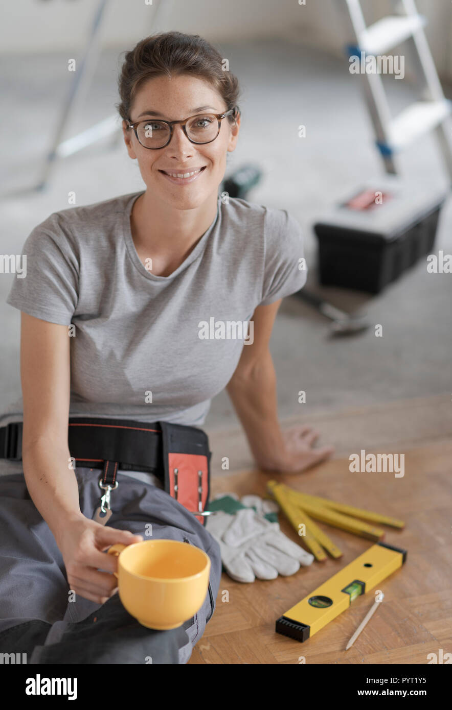 Young smiling woman having a coffee break and sitting on the floor, she ...