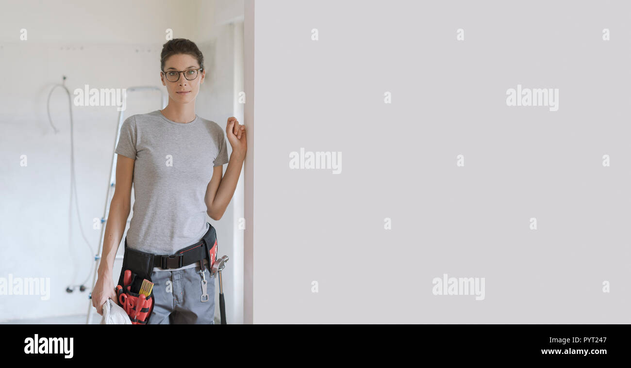 Confident female contractor posing with tool belt and smiling at camera ...