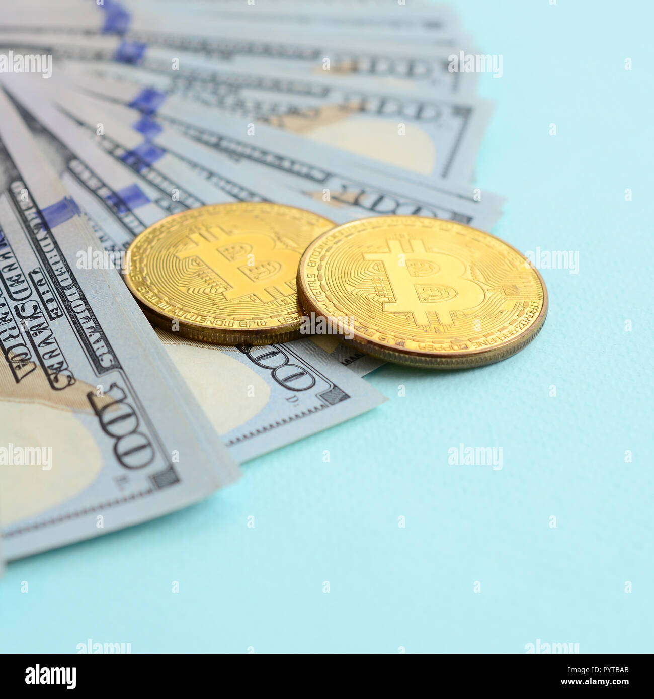 Golden bitcoins and hundred dollar bills lies on light blue background ...