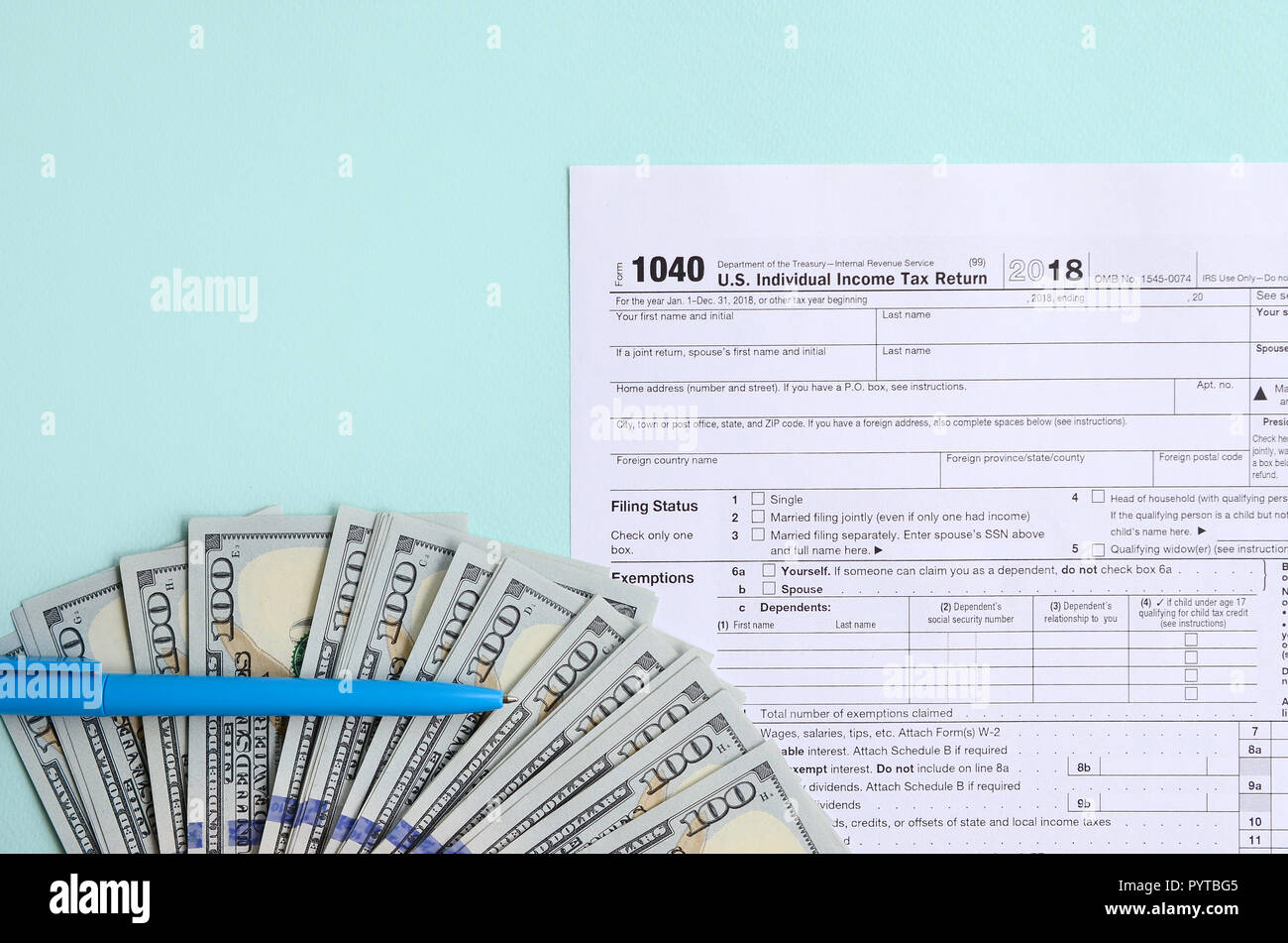 1040 tax form lies near hundred dollar bills and blue pen on a light ...
