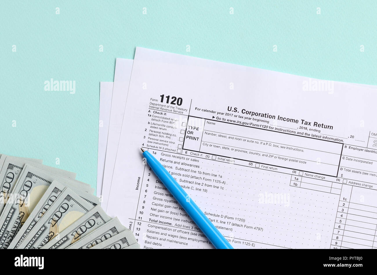 1120 tax form lies near hundred dollar bills and blue pen on a light blue background. US ...