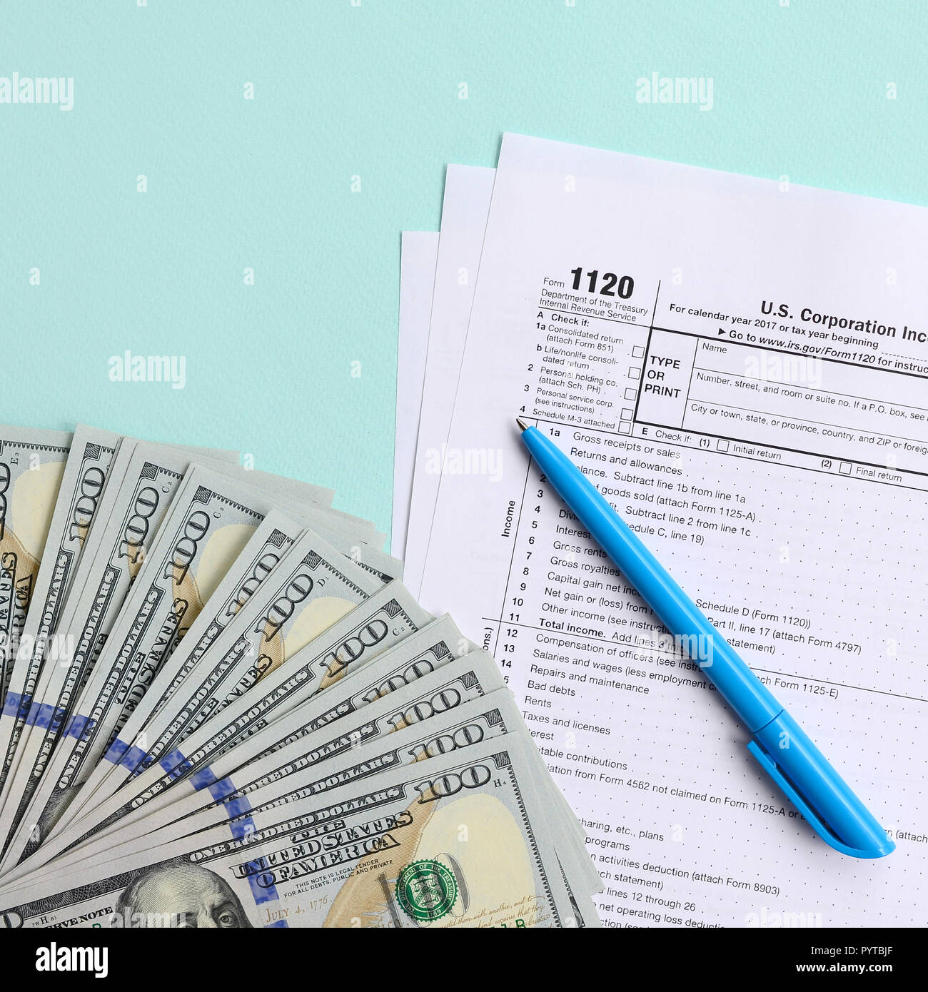 1120 tax form lies near hundred dollar bills and blue pen on a light blue background. US ...