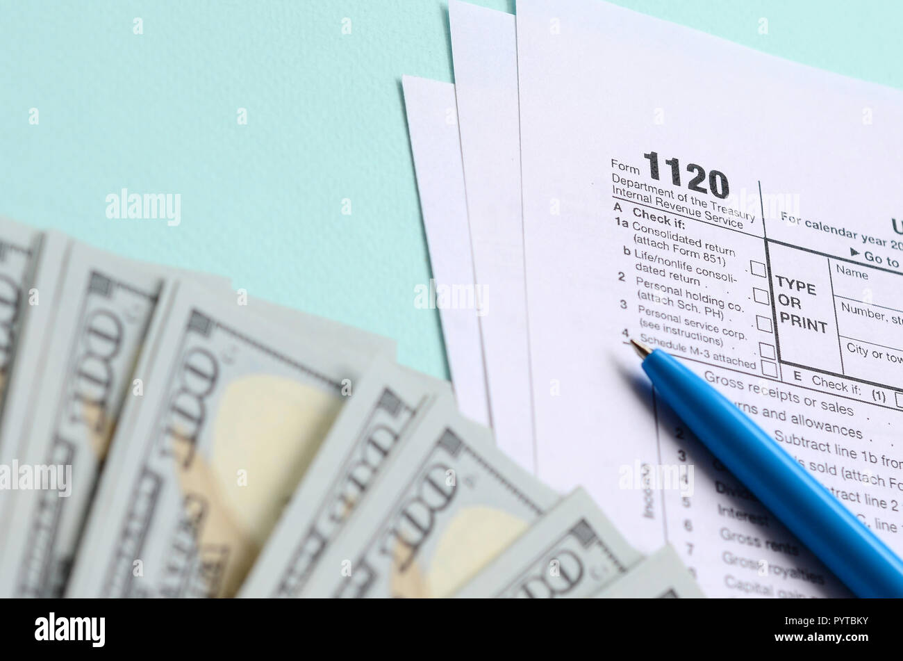 1120 tax form lies near hundred dollar bills and blue pen on a light blue background. US ...