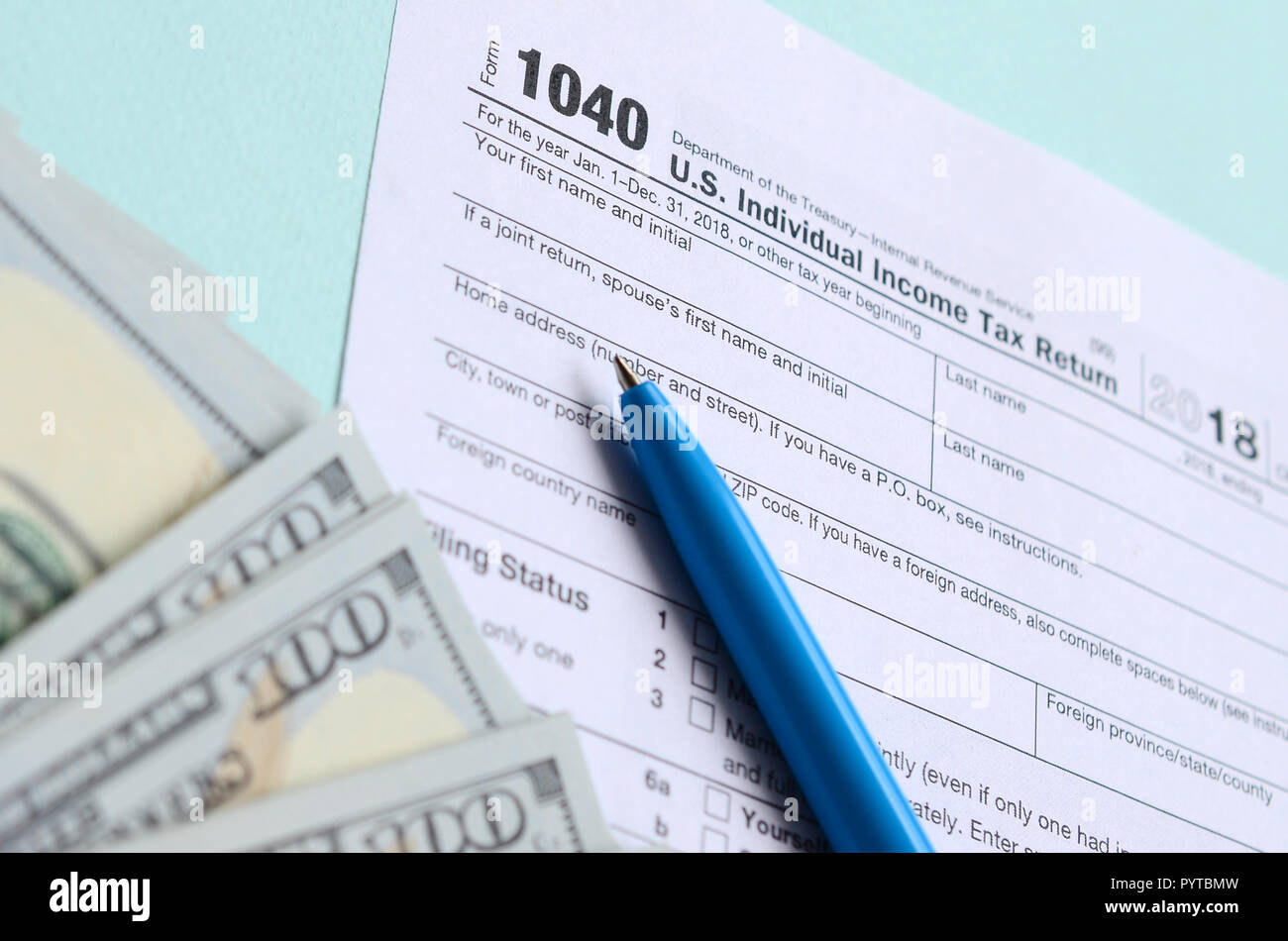 1040 tax form lies near hundred dollar bills and blue pen on a light ...