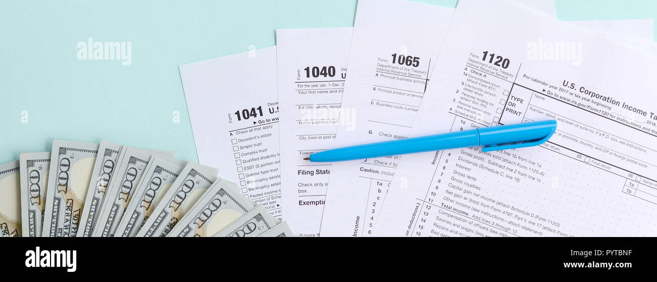 Tax forms lies near hundred dollar bills and blue pen on a light blue ...