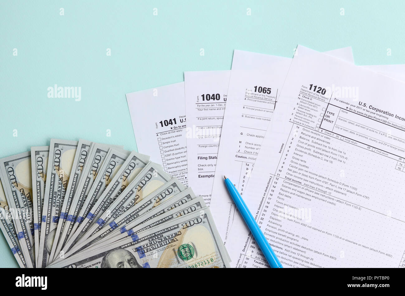 Tax forms lies near hundred dollar bills and blue pen on a light blue ...