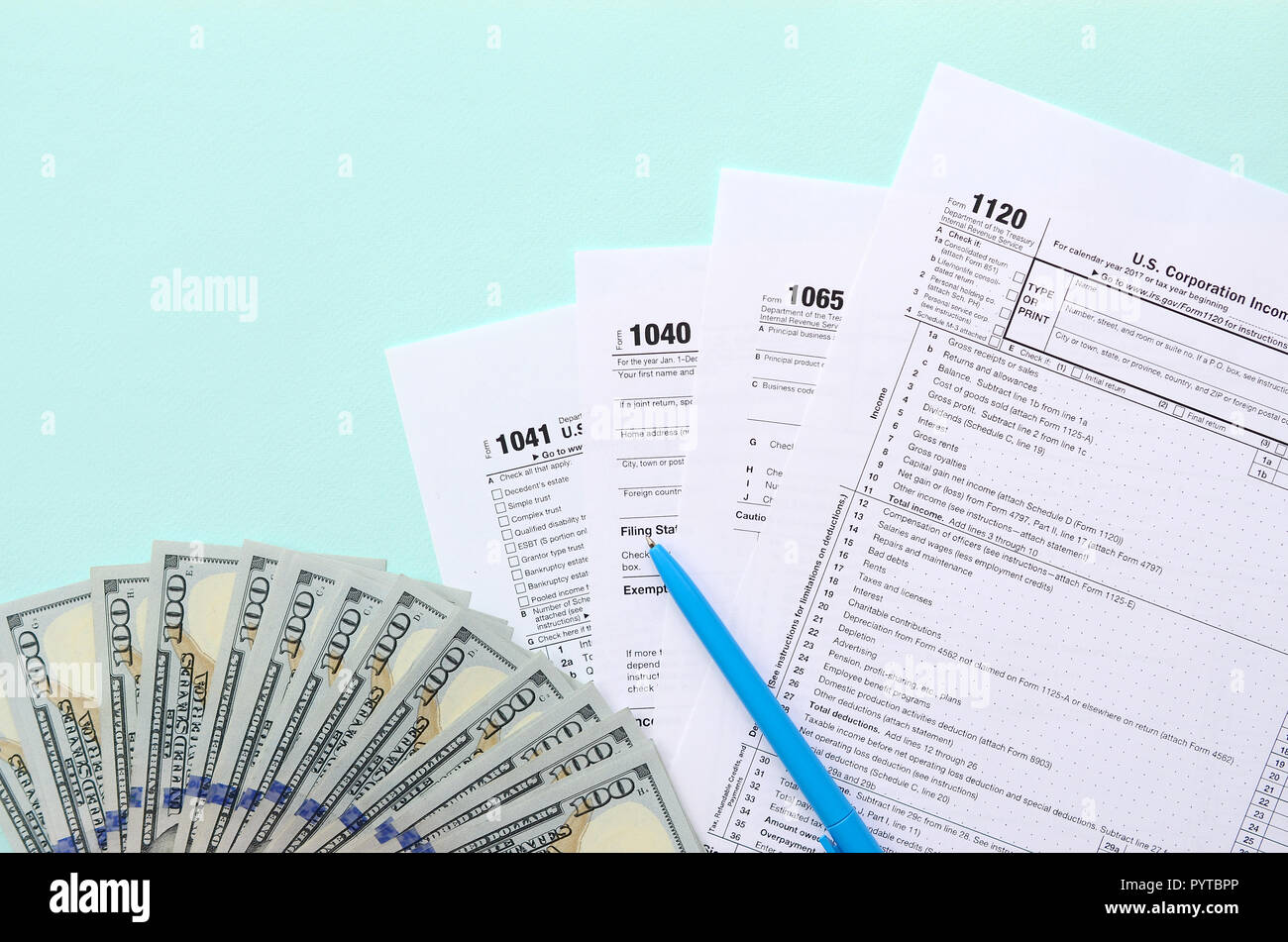 Tax forms lies near hundred dollar bills and blue pen on a light blue ...