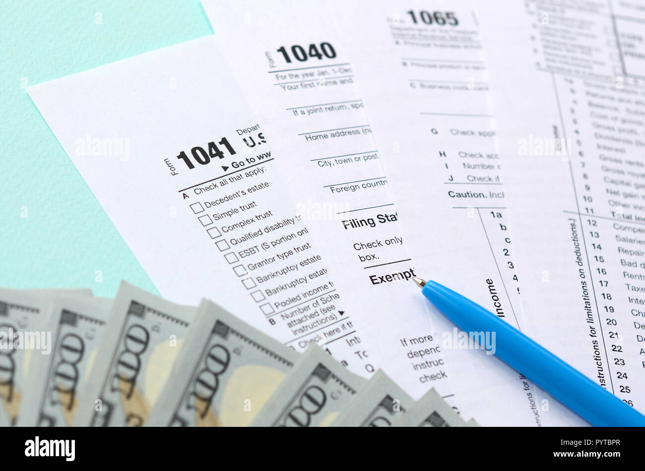 Tax forms lies near hundred dollar bills and blue pen on a light blue ...