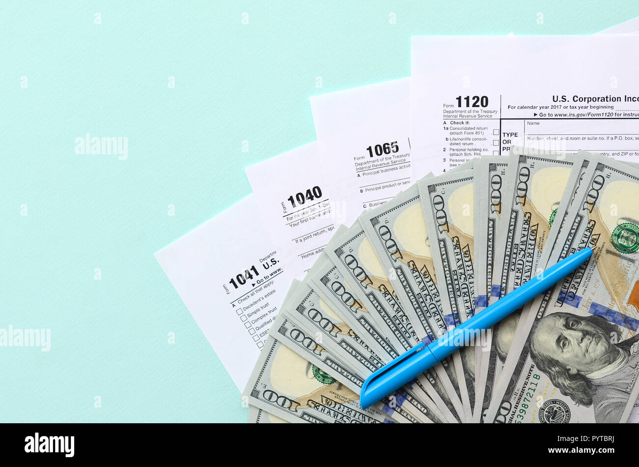 Tax forms lies near hundred dollar bills and blue pen on a light blue ...