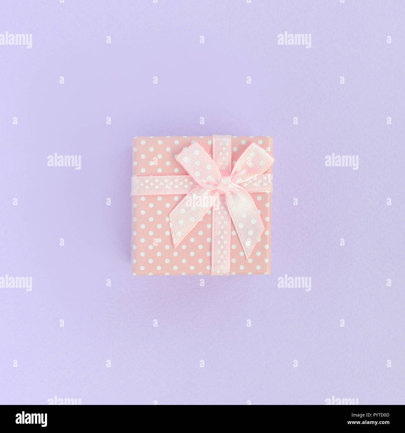 Small pink gift box with ribbon lies on a violet background. Minimalism ...