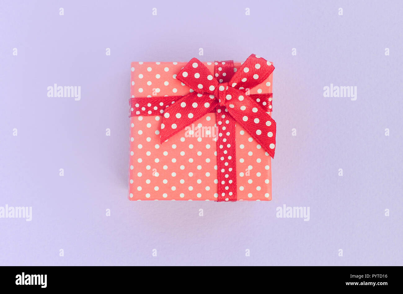 Small red gift box with ribbon lies on a violet background. Minimalism ...