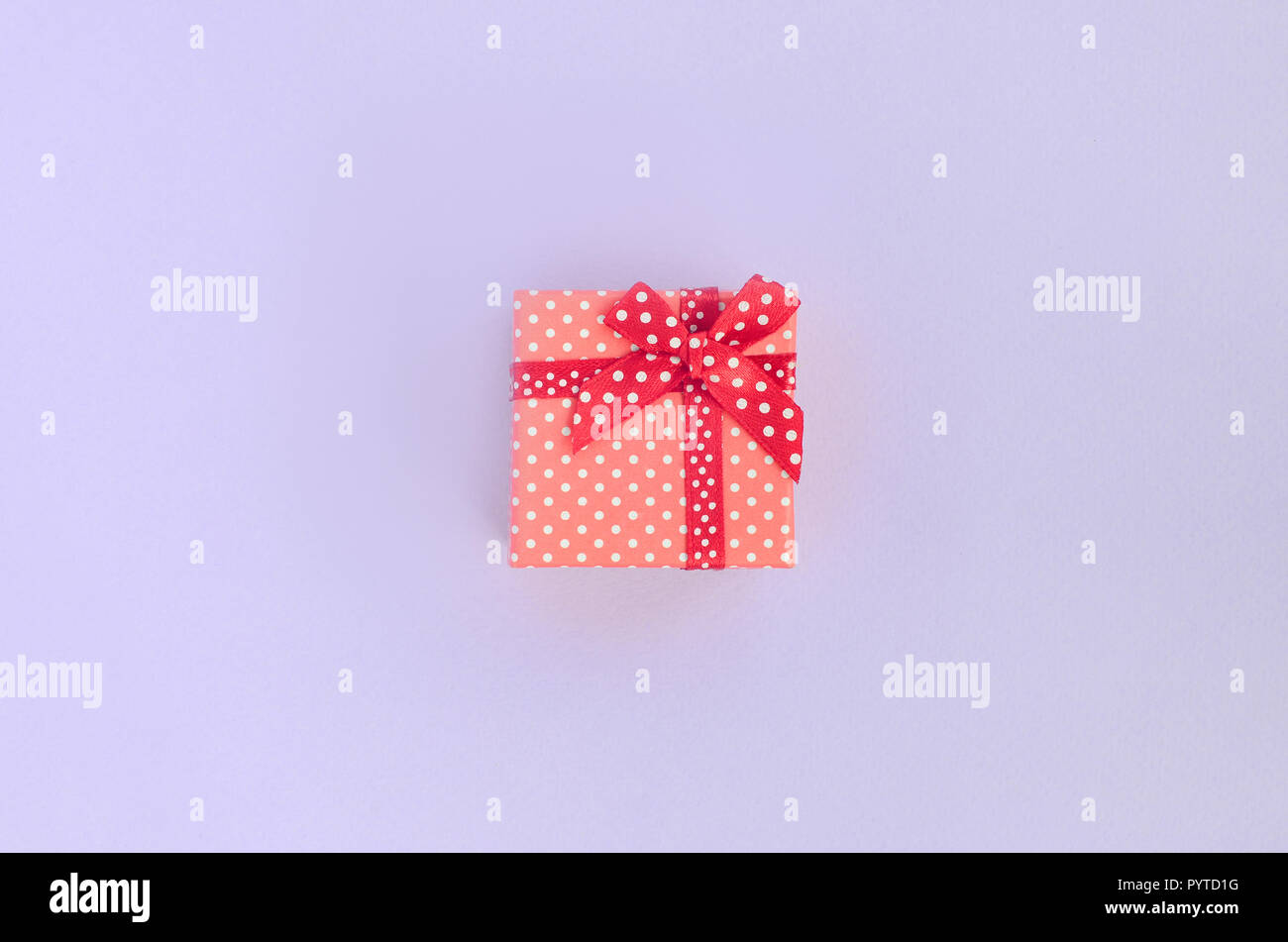 Small red gift box with ribbon lies on a violet background. Minimalism ...
