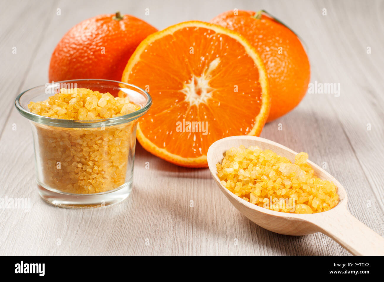 Cut orange with two whole oranges, glass bowl and wooden spoon with yellow sea salt on wooden ...