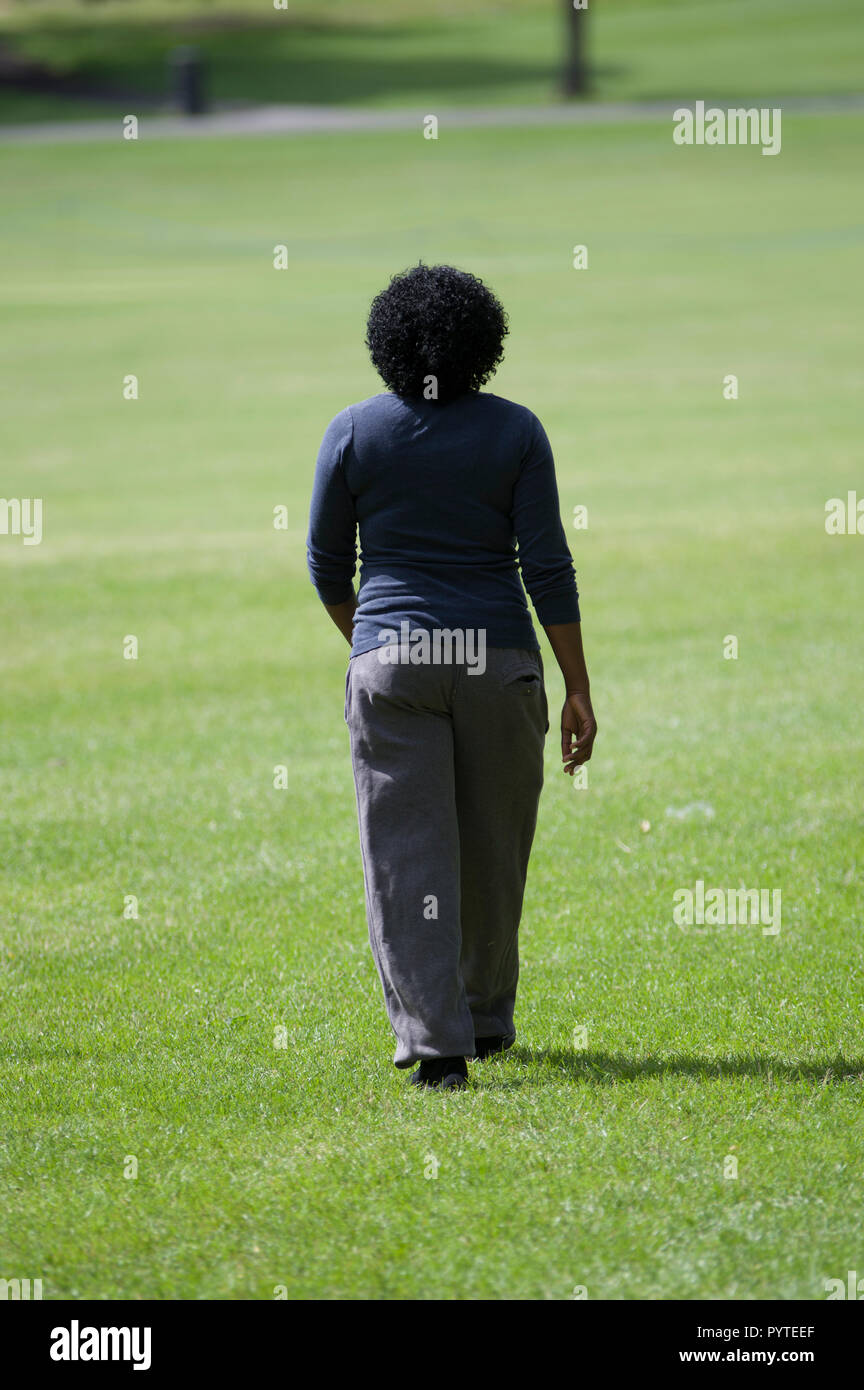 African Or Caribbean Woman Walking Away In The Grass In Springfield
