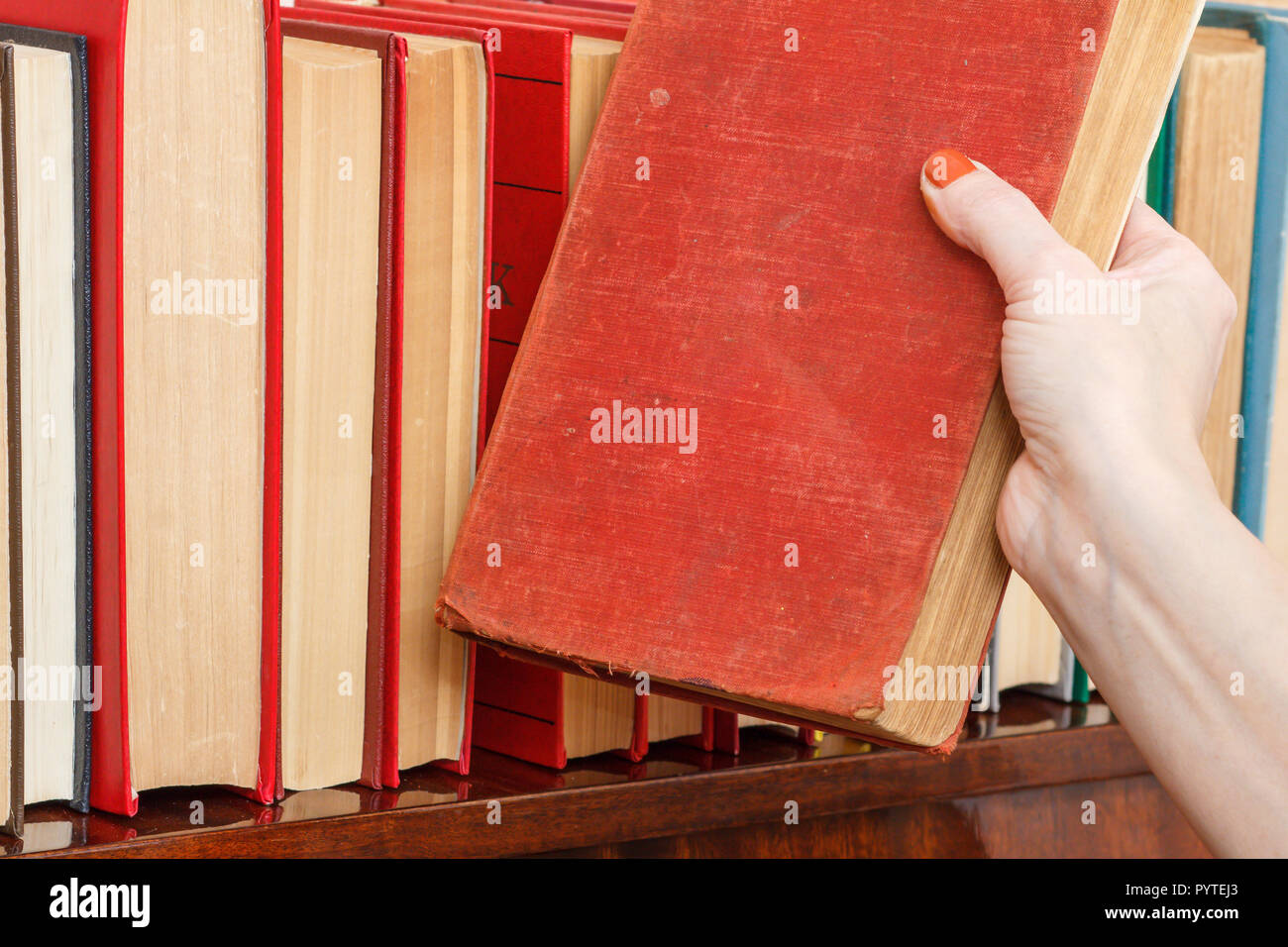 Female hand is taking a book from a bookshelf. Many hardback books on ...
