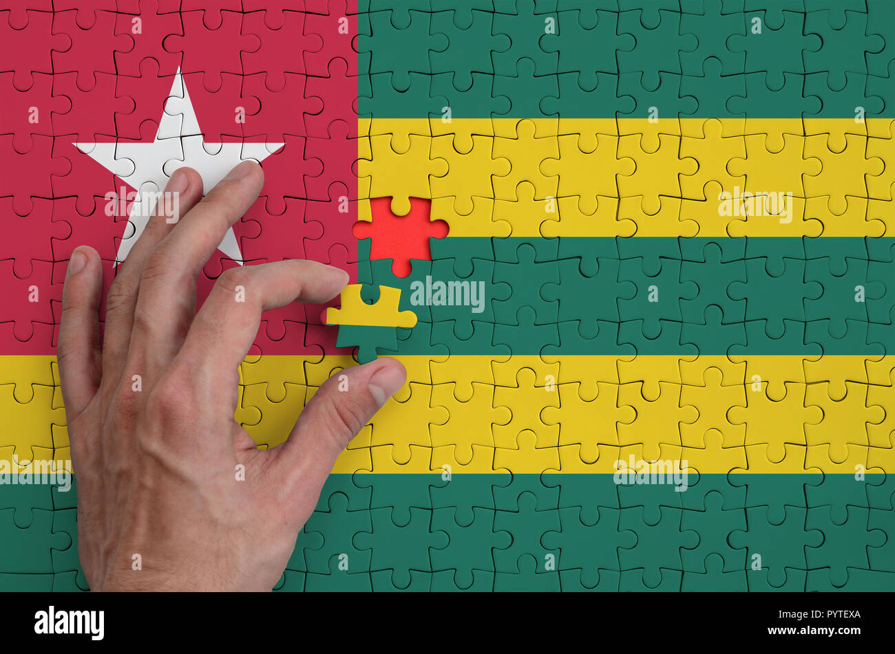 Togo flag is depicted on a puzzle, which the man's hand completes to ...